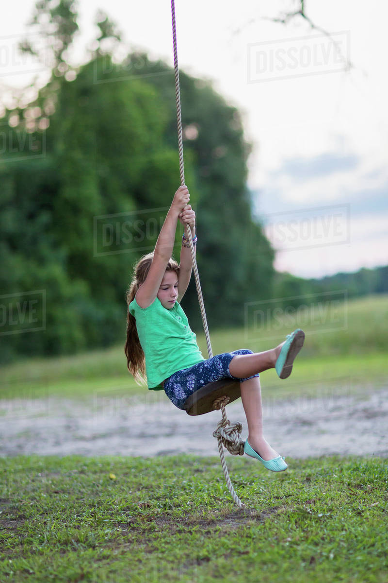 Caucasian girl playing on rope swing - Royalty-free Stock Photo | Dissolve