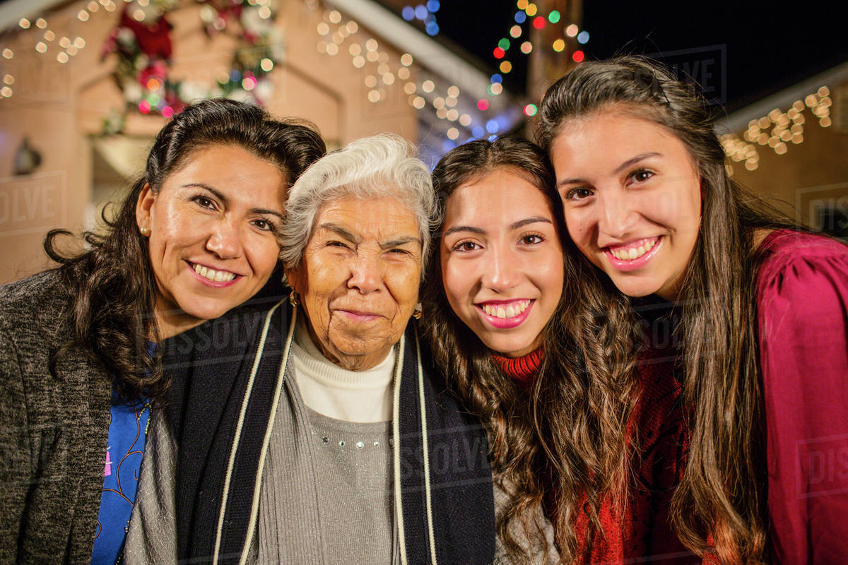 Three generations of Hispanic women standing outside house decorated ...