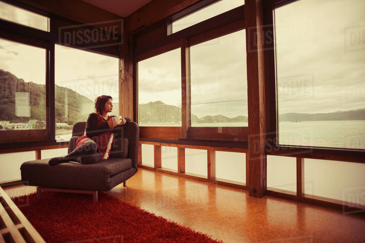 Mixed race woman looking out window of modern house - Royalty-free ...