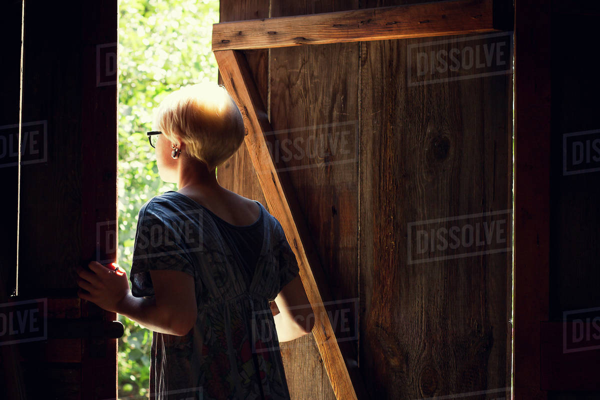 Caucasian woman looking out barn door - Royalty-free Stock Photo | Dissolve