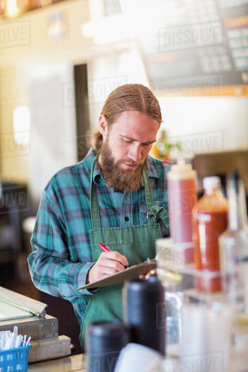 Caucasian server writing on clipboard in cafe - Stock Photo - Dissolve