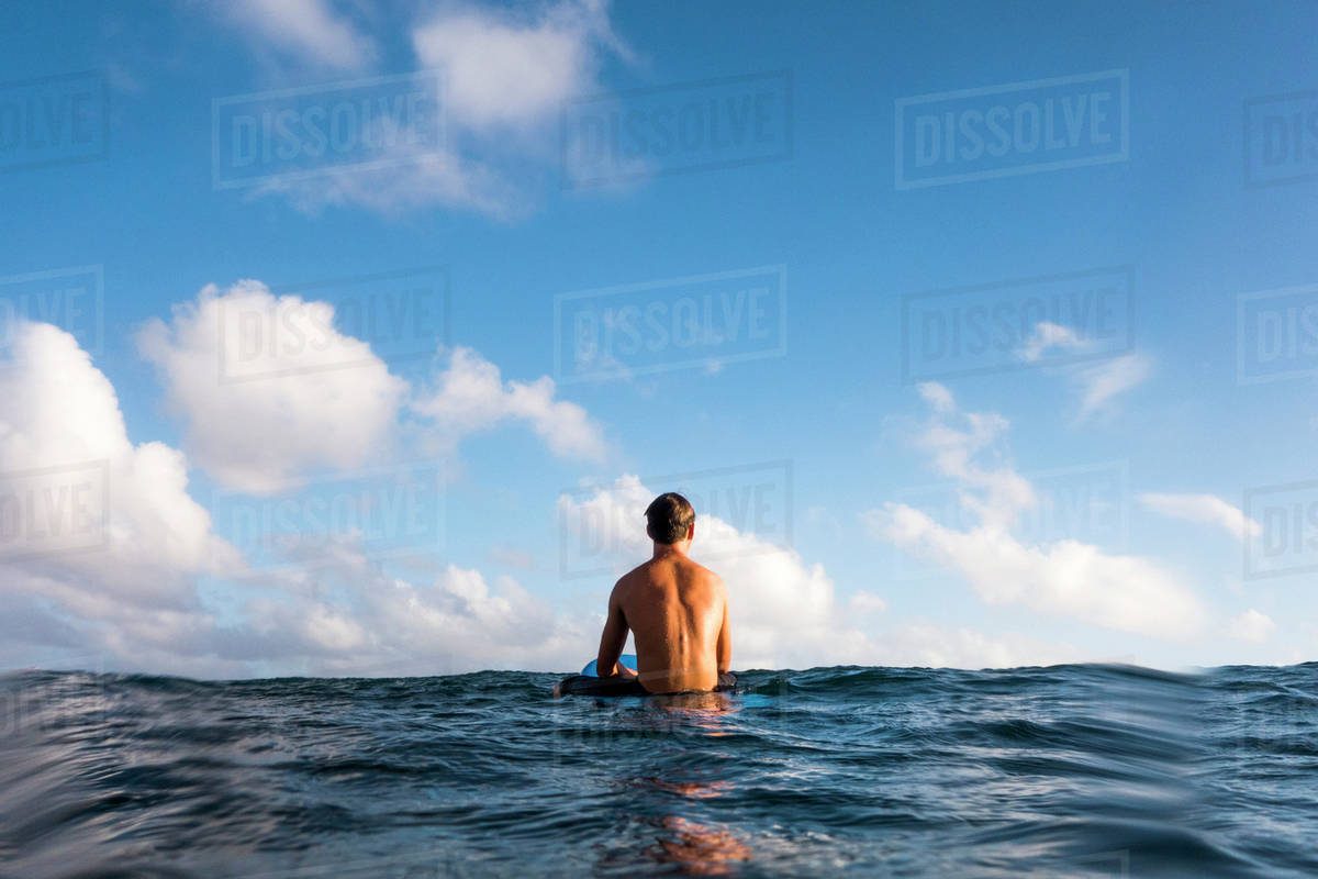 Surfer sitting on surfboard in ocean - Stock Photo - Dissolve