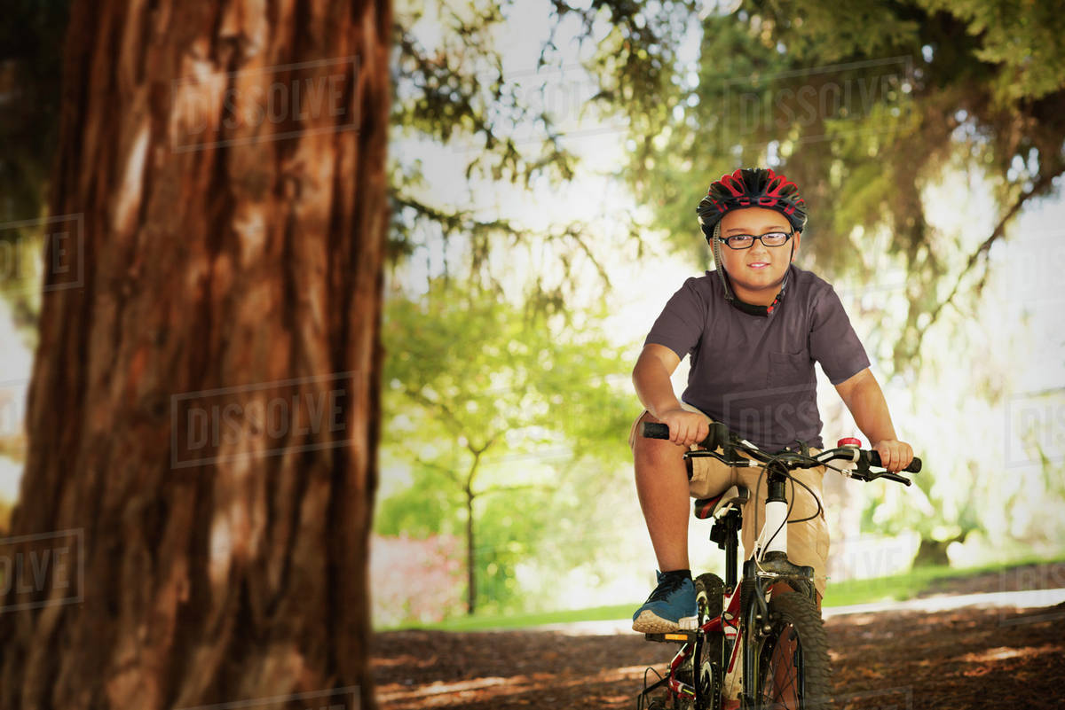 Mixed race boy riding mountain bike in forest - Stock Photo - Dissolve