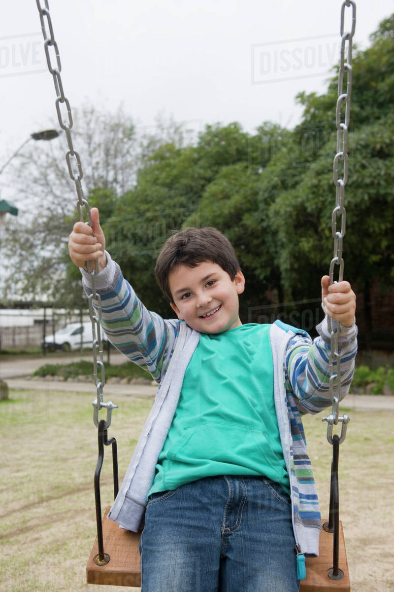 Hispanic boy playing on swing - Royalty-free Stock Photo | Dissolve