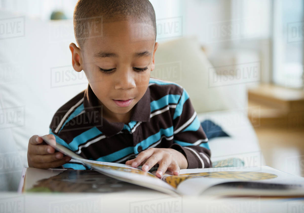 African American boy reading book on sofa - Royalty-free Stock Photo ...