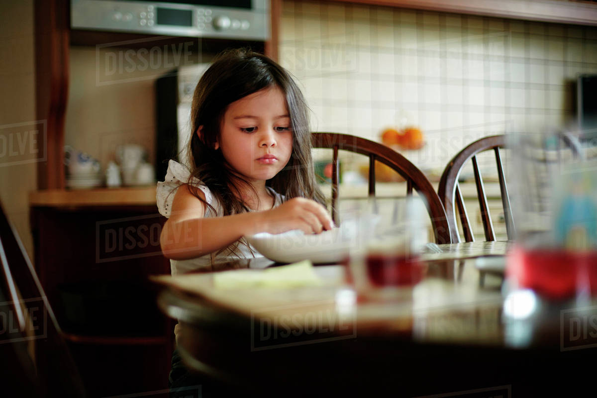 Caucasian girl eating at kitchen table - Stock Photo - Dissolve