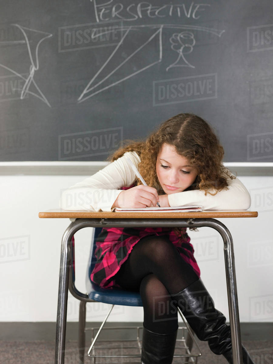 Student writing notes at desk in classroom - Stock Photo - Dissolve