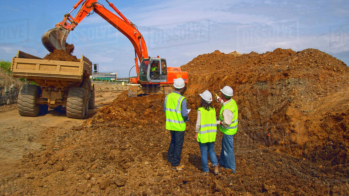 Workers watching digger machinery in field - Stock Photo - Dissolve