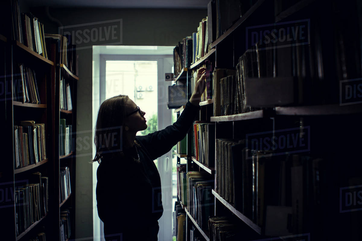 Caucasian woman searching for book in library - Royalty-free Stock ...