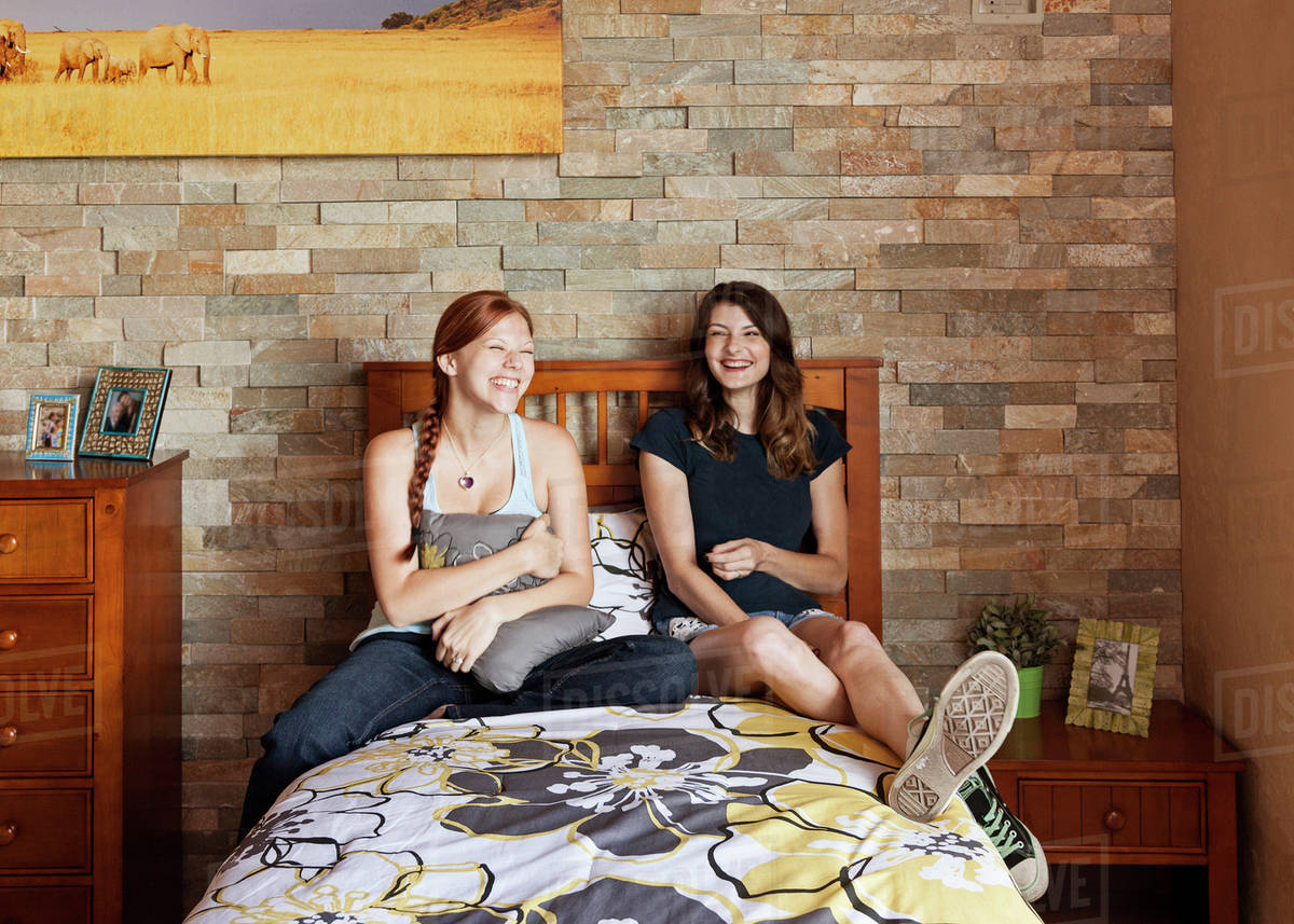 Students laughing on bed in dorm room - Stock Photo - Dissolve