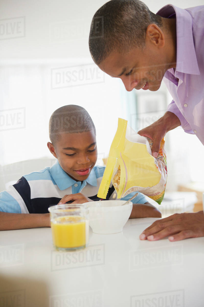 Mixed race man pouring cereal for son - Royalty-free Stock Photo | Dissolve