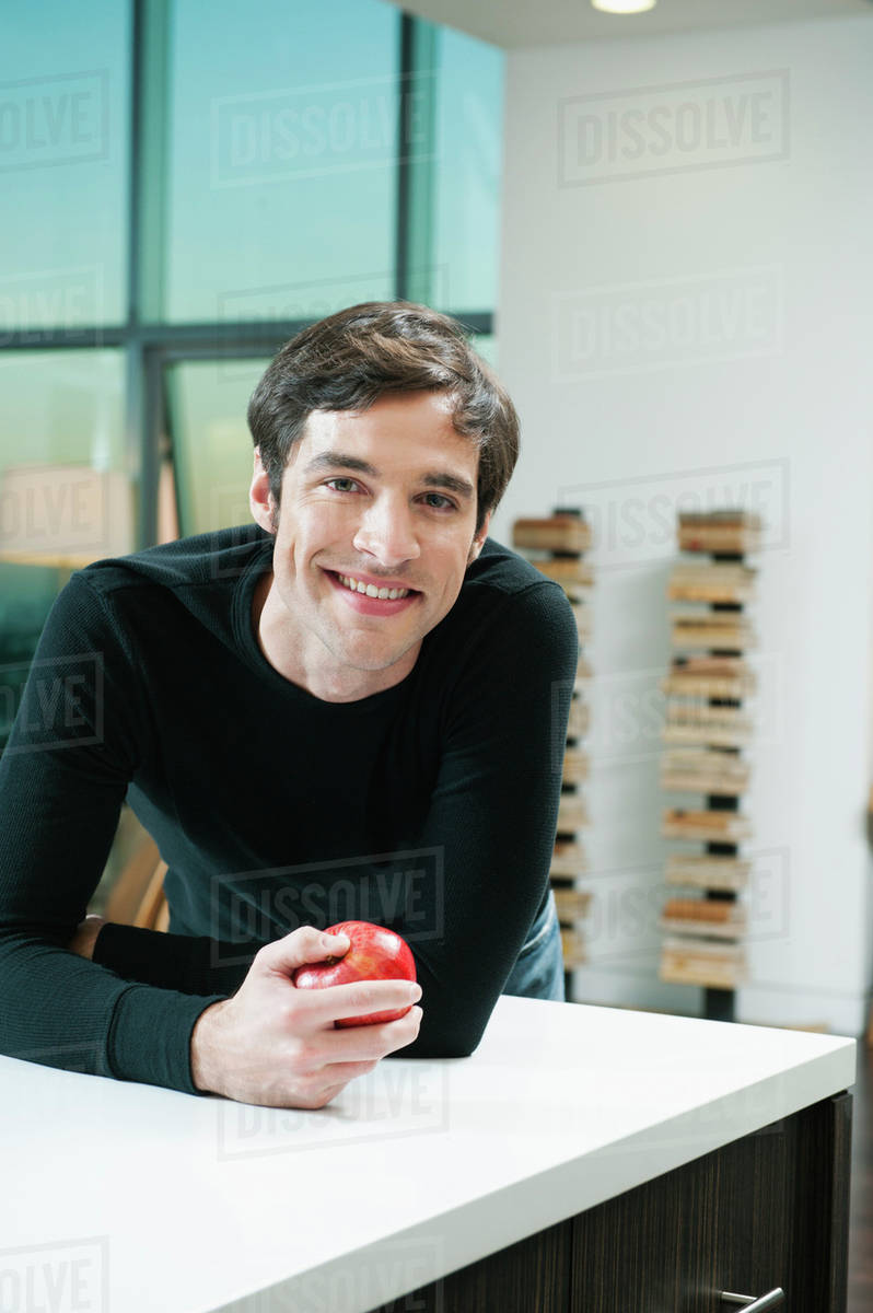 Caucasian man leaning on counter holding apple - Stock Photo - Dissolve