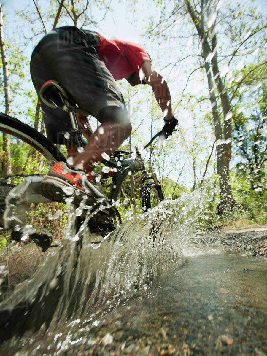 Mixed race man riding mountain bike through stream - Royalty-free Stock ...
