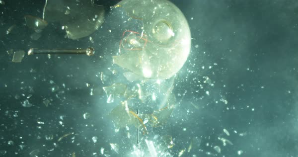 Extreme closeup of a light bulb exploding, sending shards of glass and ...