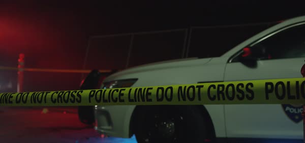 Medium shot of police line tape at crime scene, police car parked in ...