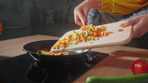 Closeup woman pouring out chopped vegetables in a hot frying pan ...