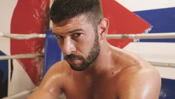 Sweaty male boxer sitting inside boxing ring breathing heavily tired ...