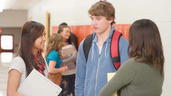A small group of students stand in a high school hallway and talk to ...