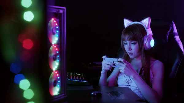 Cute gamer girl sitting by PC illuminated with neon lights and playing ...