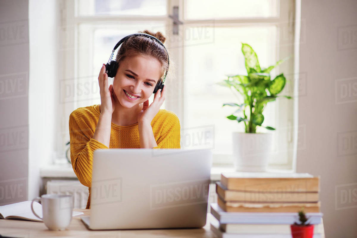 A young happy college female student sitting at the table at home ...