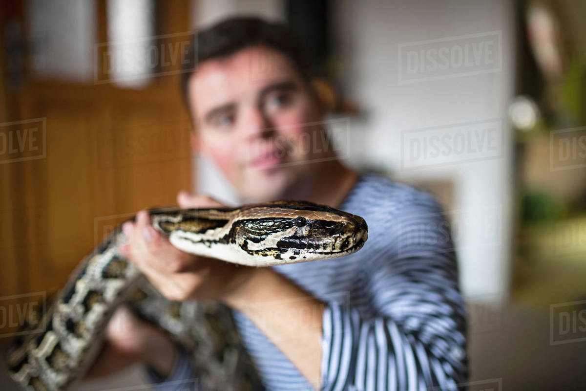 Portrait of down syndrome adult man sitting indoors in bedroom at home ...