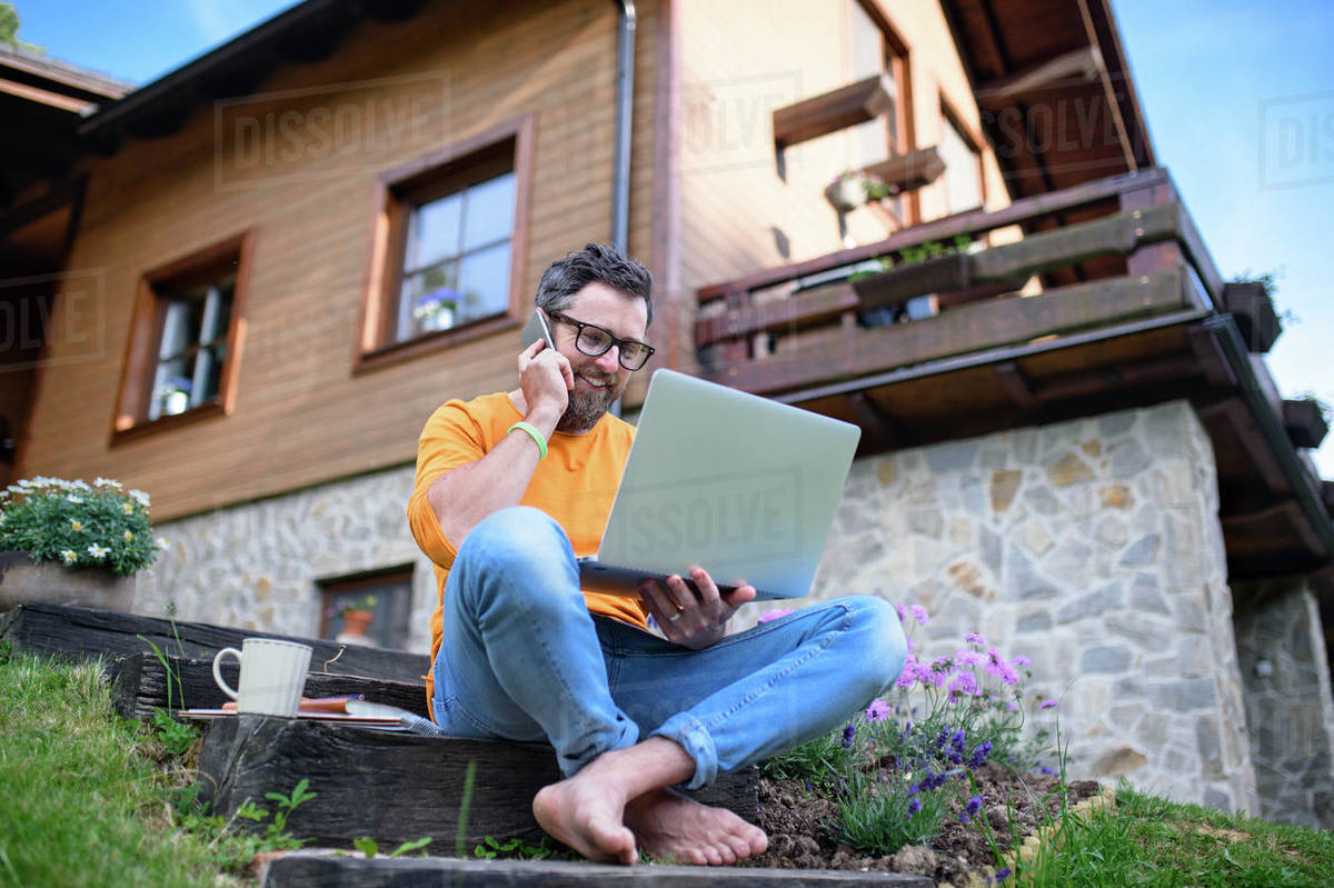 Portrait of mature man with laptop and smartphone working outdoors in ...