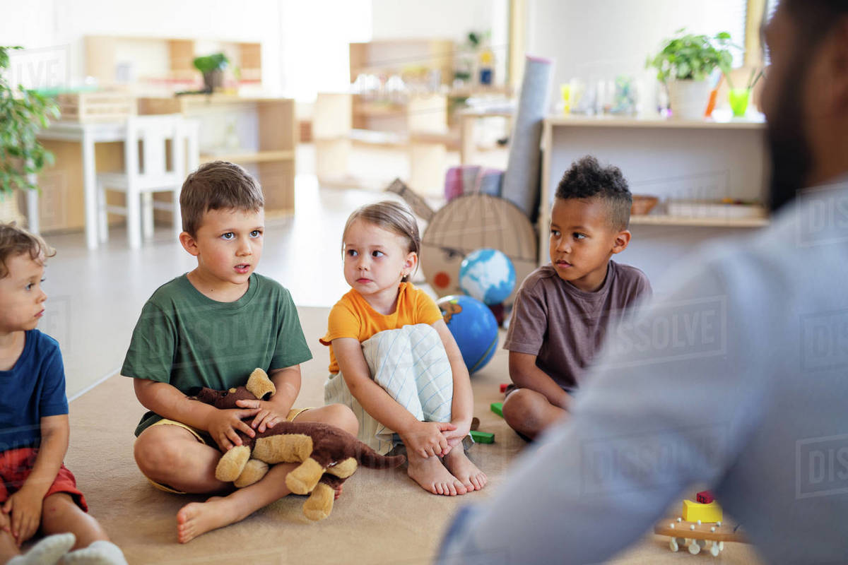 A group of small nursery school children sitting on floor indoors in ...