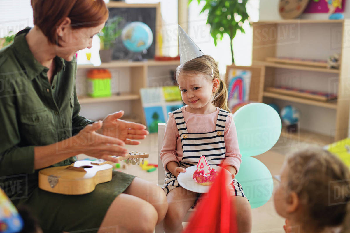 A group of small nursery school children with teacher on floor indoors ...
