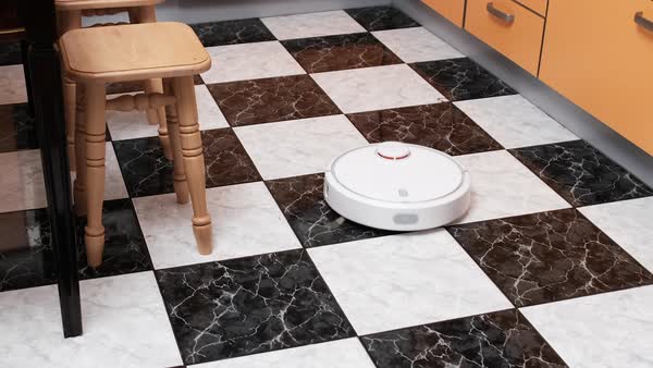 Robot Cleaner Cleans in the House at Kitchen. Modern round vacuum robot ...