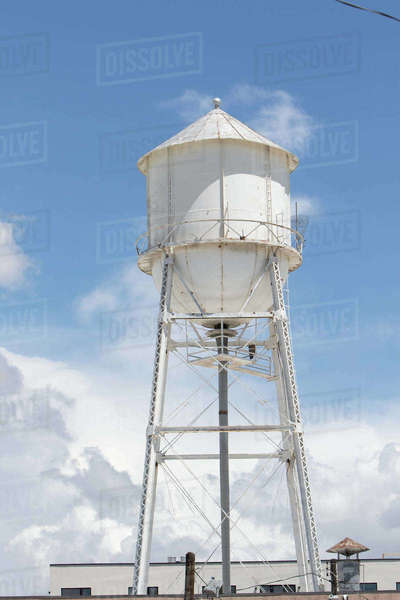 A white water tower mounted on the top of a building against a cloudy ...