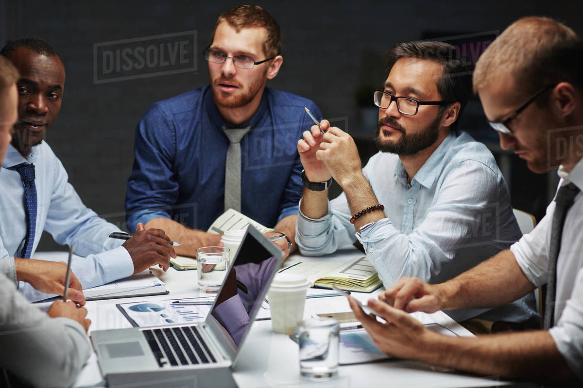 Group of serious managers looking at colleague explaining idea ...