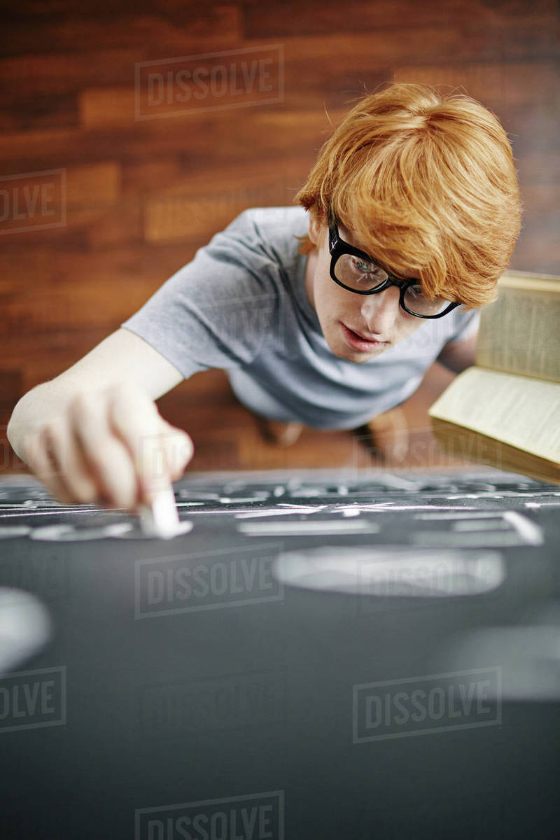 Student with book writing on blackboard with chalk - Stock Photo - Dissolve