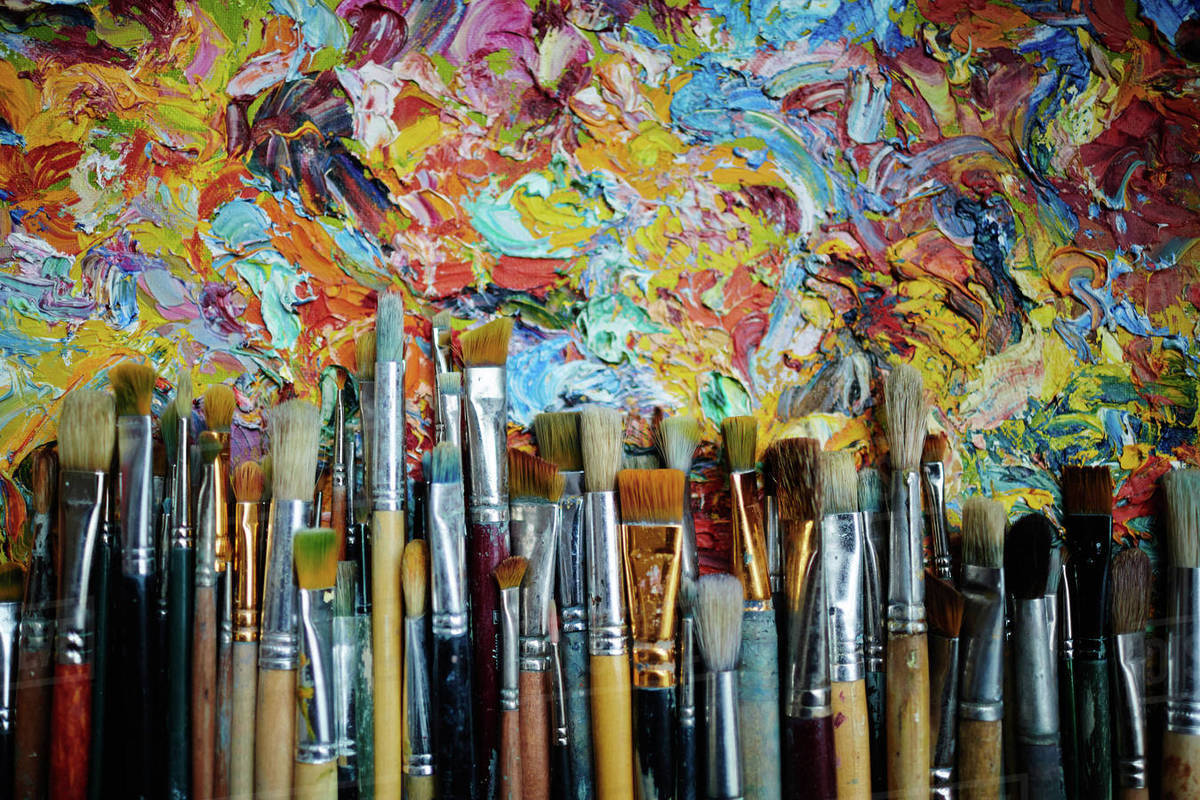 Top view of rows of paintbrushes laying on abstract colorful oil paint ...