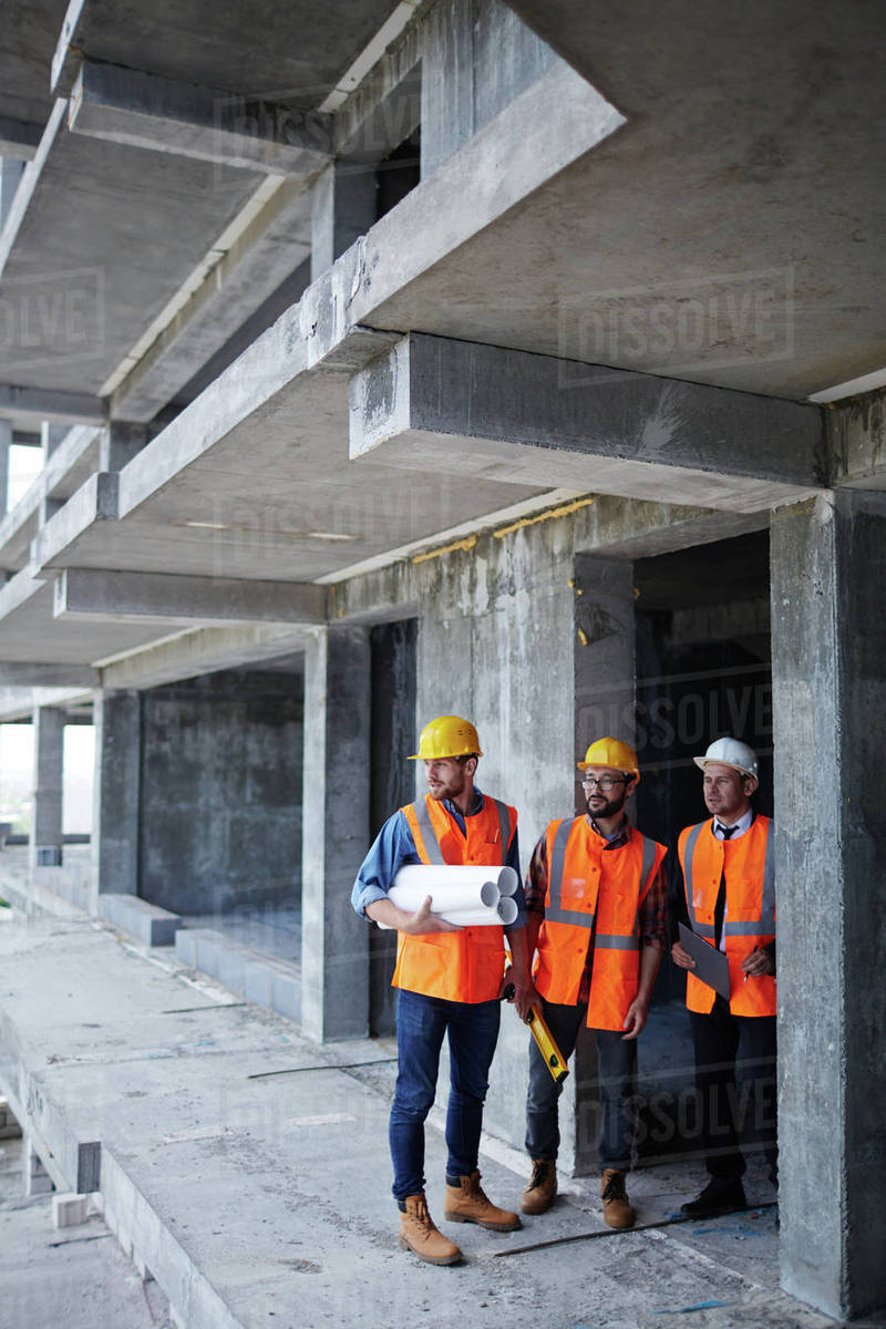 Inspectors in helmets and uniform standing by unfinished construction ...