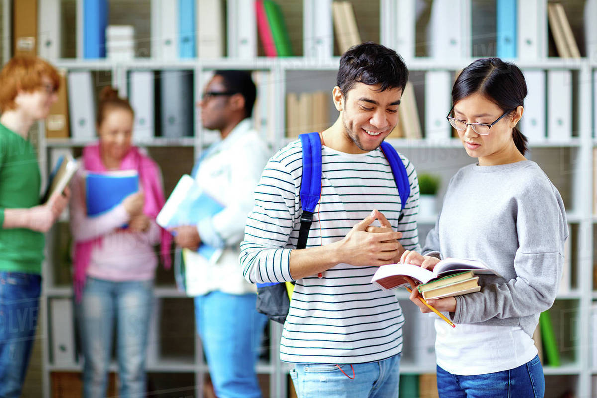College students looking at page of book or dictionary in library ...