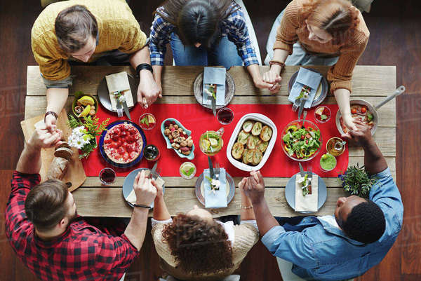 Friends sitting at dinner table holding hands - Royalty-free Stock ...