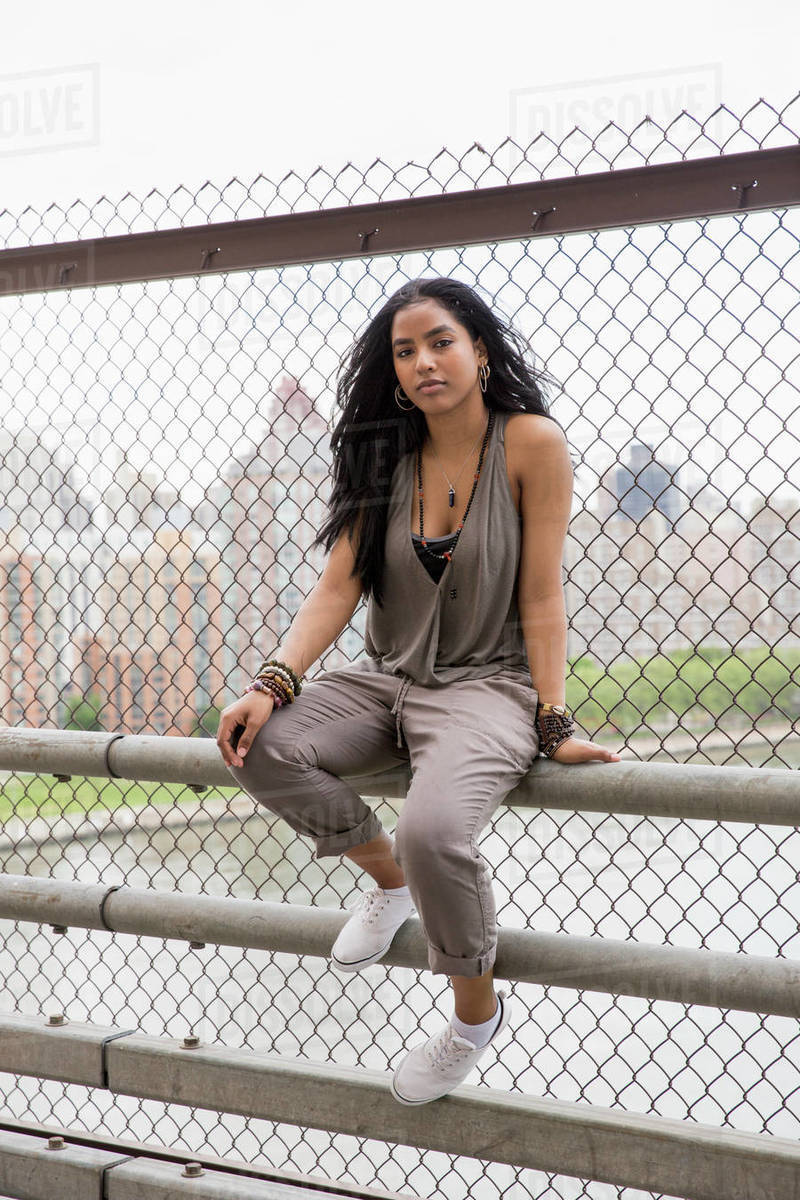 Young woman sitting on a railing on a bridge - Stock Photo - Dissolve