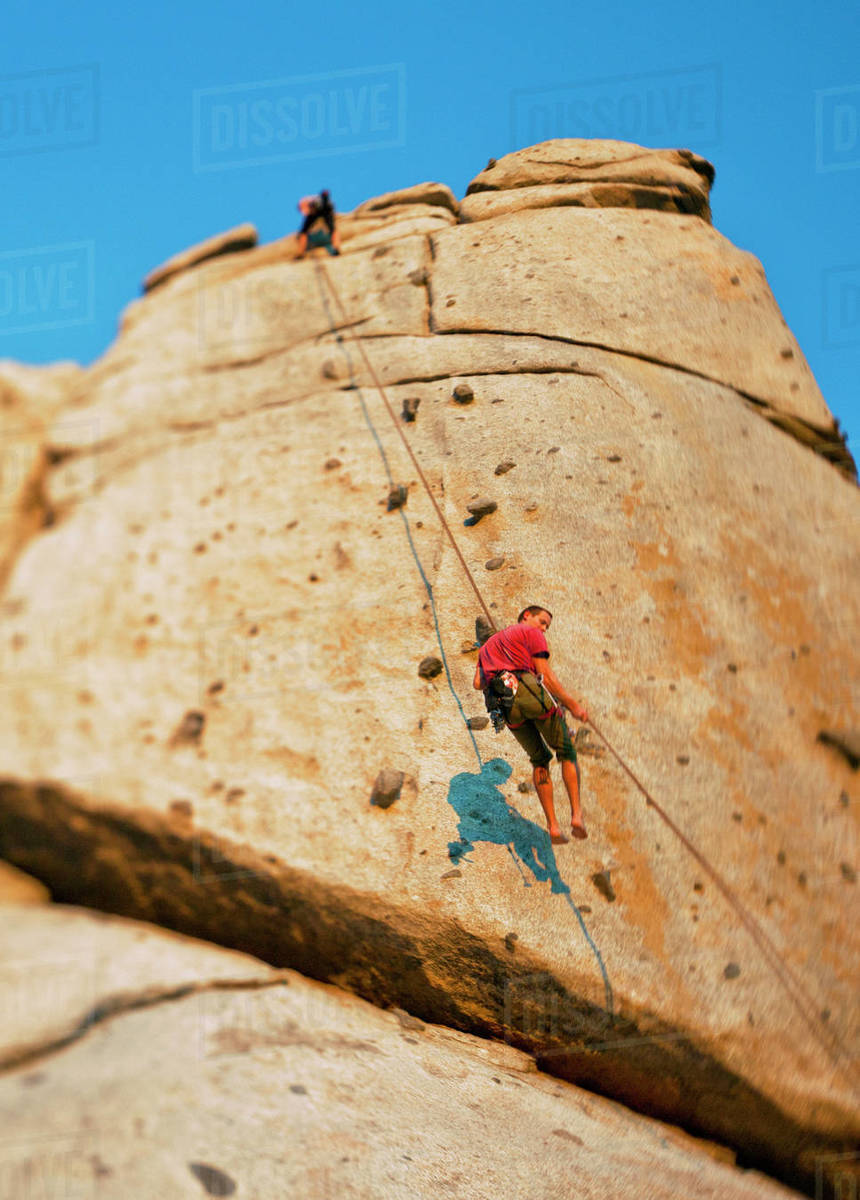 Low-angle view of two rock climbers climbing on mountain top. - Royalty ...