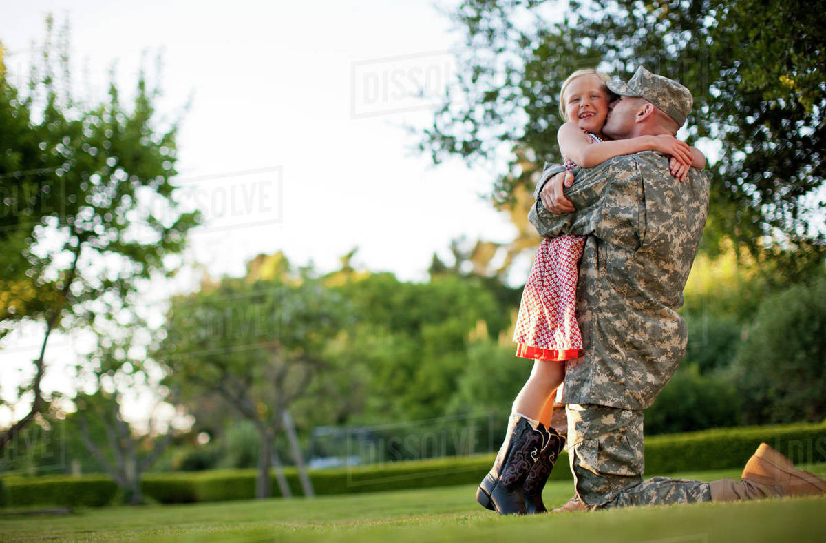 Male soldier hugging his young daughter in the back yard of their home ...