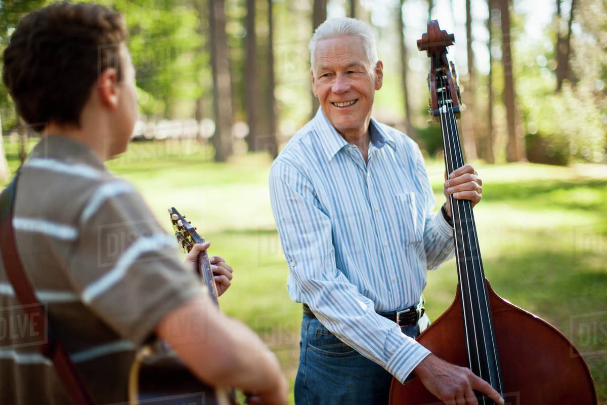 Smiling senior man playing a double bass while his grandson plays an ...