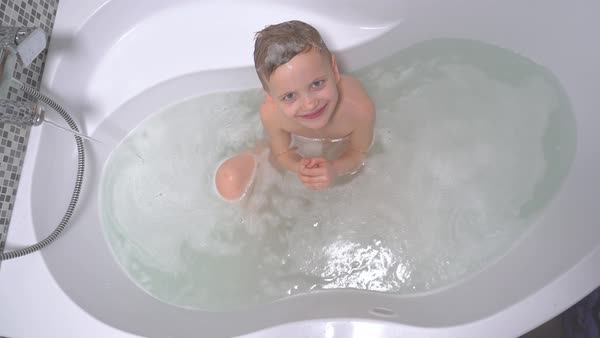 6-7 Years old boy taking a bath, playing with foam, looking at the ...