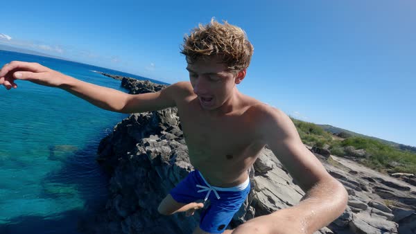 Young happy man cliff jumping off extreme ledge into tropical blue ...