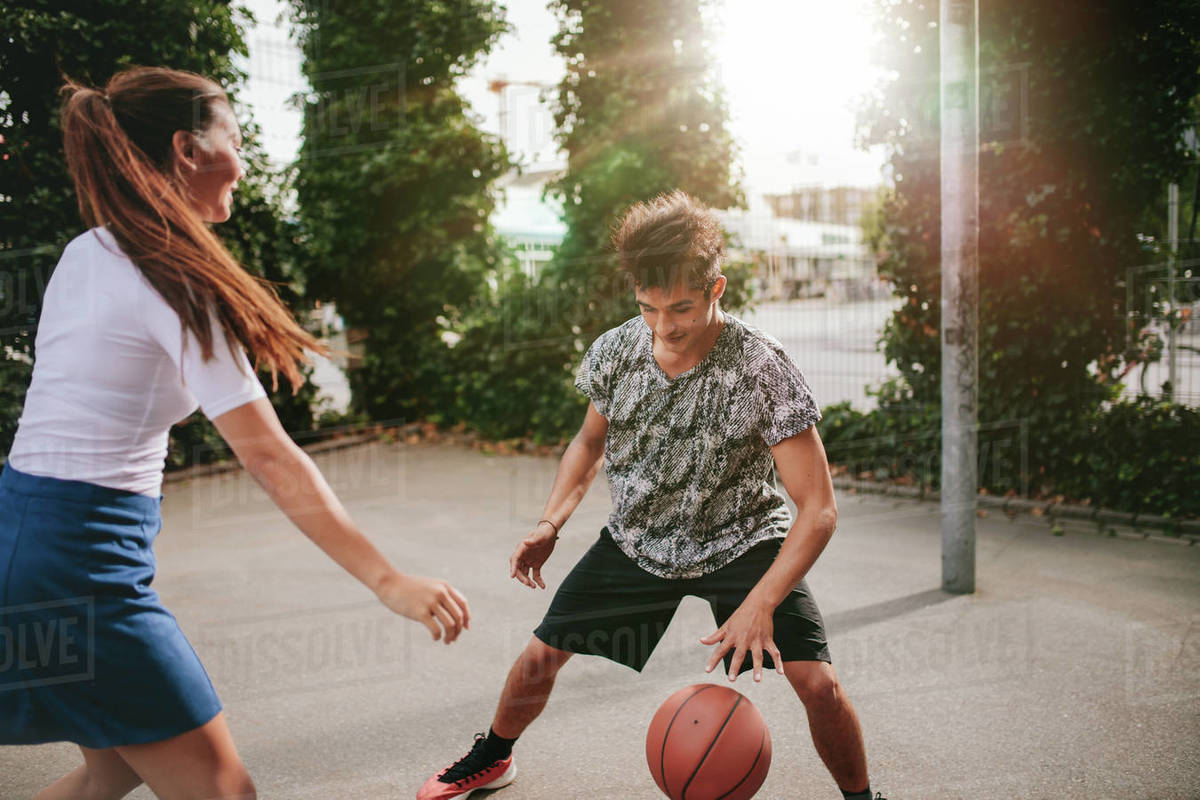 Two young man and woman on basketball court dribbling with ball ...