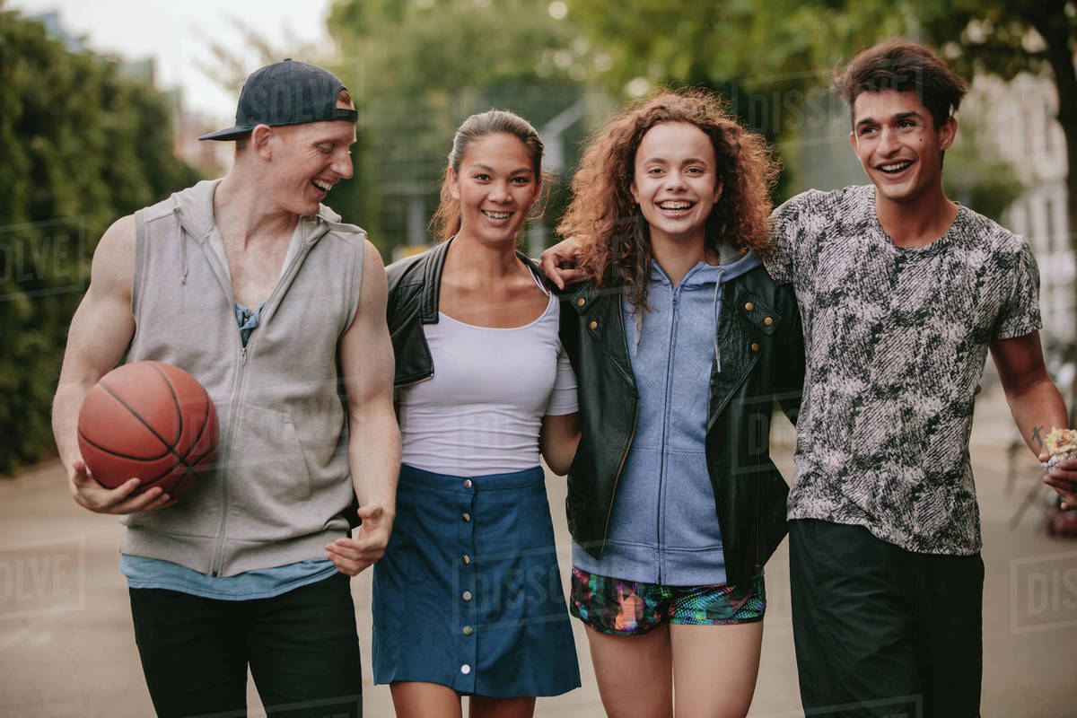 Portrait of four young friends walking together and smiling. Mixed race ...