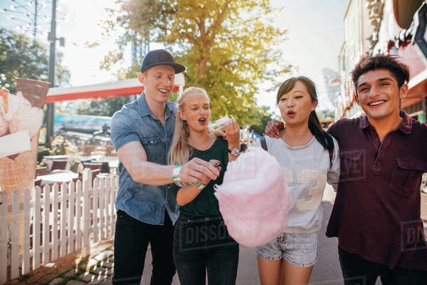 Group of friends eating cotton candy in amusement park. Young man and ...