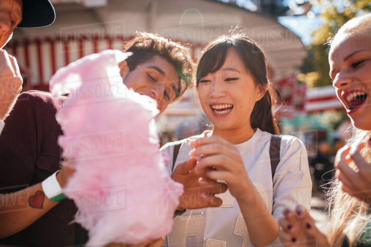 Group of friends eating candyfloss at amusement park. Smiling young ...