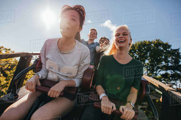 Enthusiastic young friends on roller coaster ride. Young people having ...