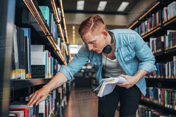 Shot of young man looking for a book in shelf. University student in ...