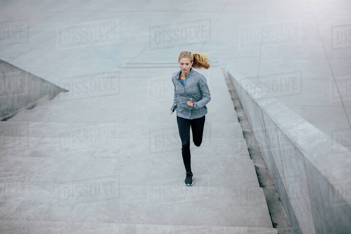 Shot of fitness female running up the steps in city. Healthy woman on ...