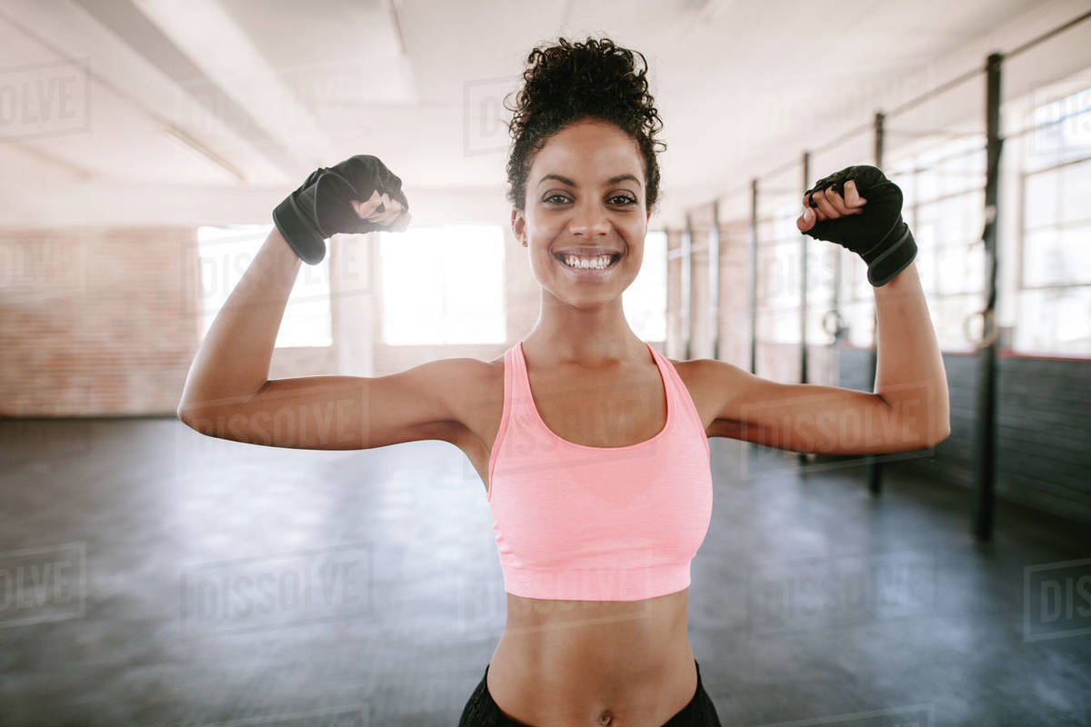 Portrait of young fitness woman flexing muscles and smiling. African ...